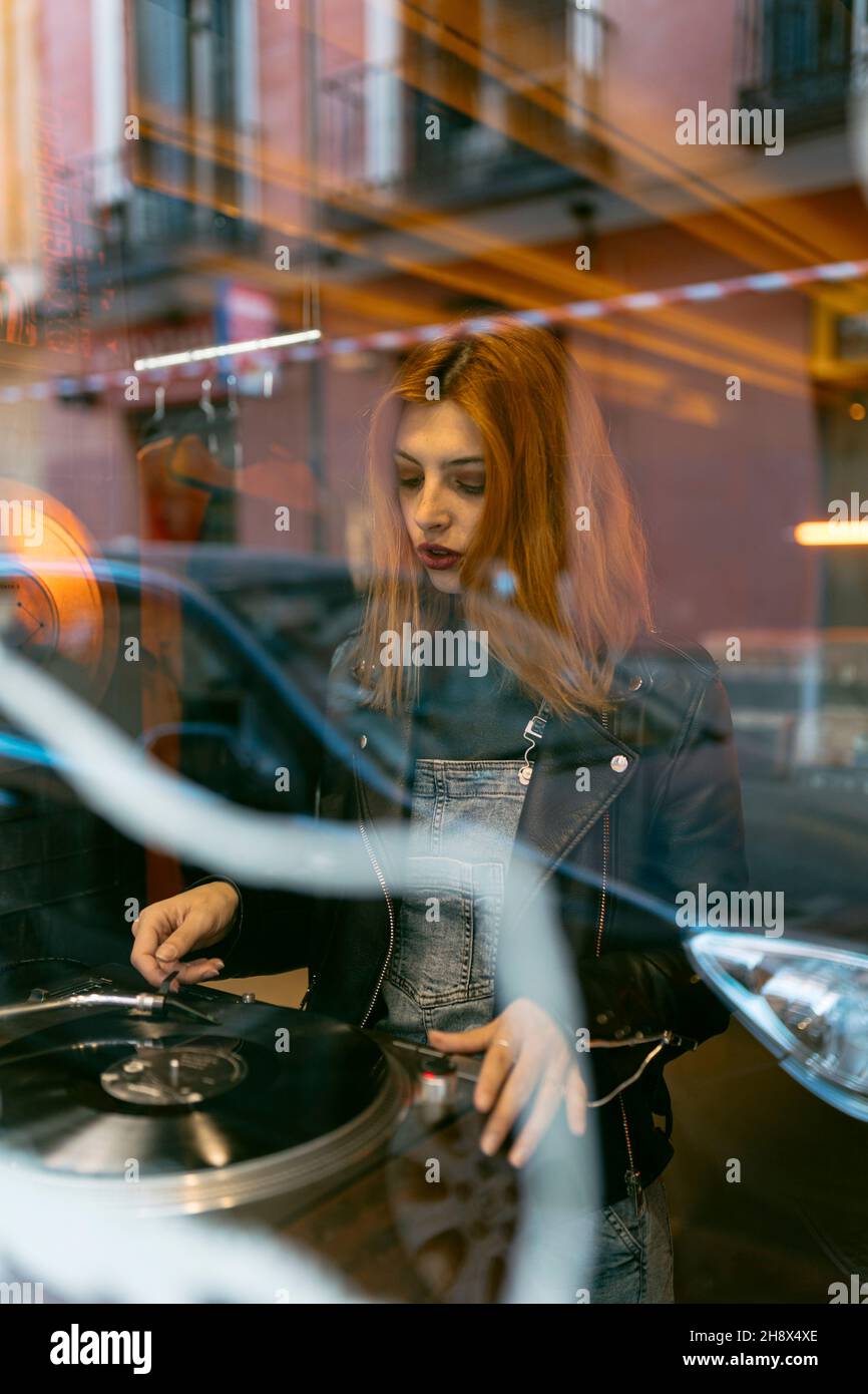 Through window of Woman playing vintage record player while standing in ...