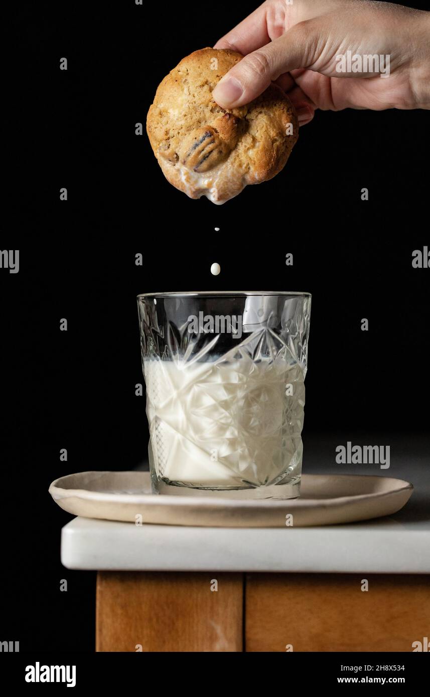 Crop anonymous person dipping fresh sweet cookie into glass of milk ...