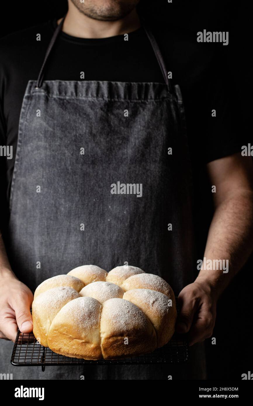 Crop unrecognizable baker standing at counter with fresh bread buns ...