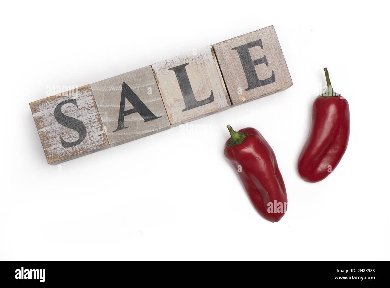 two dark red peppers next to wooden cubes representing sale isolated on ...