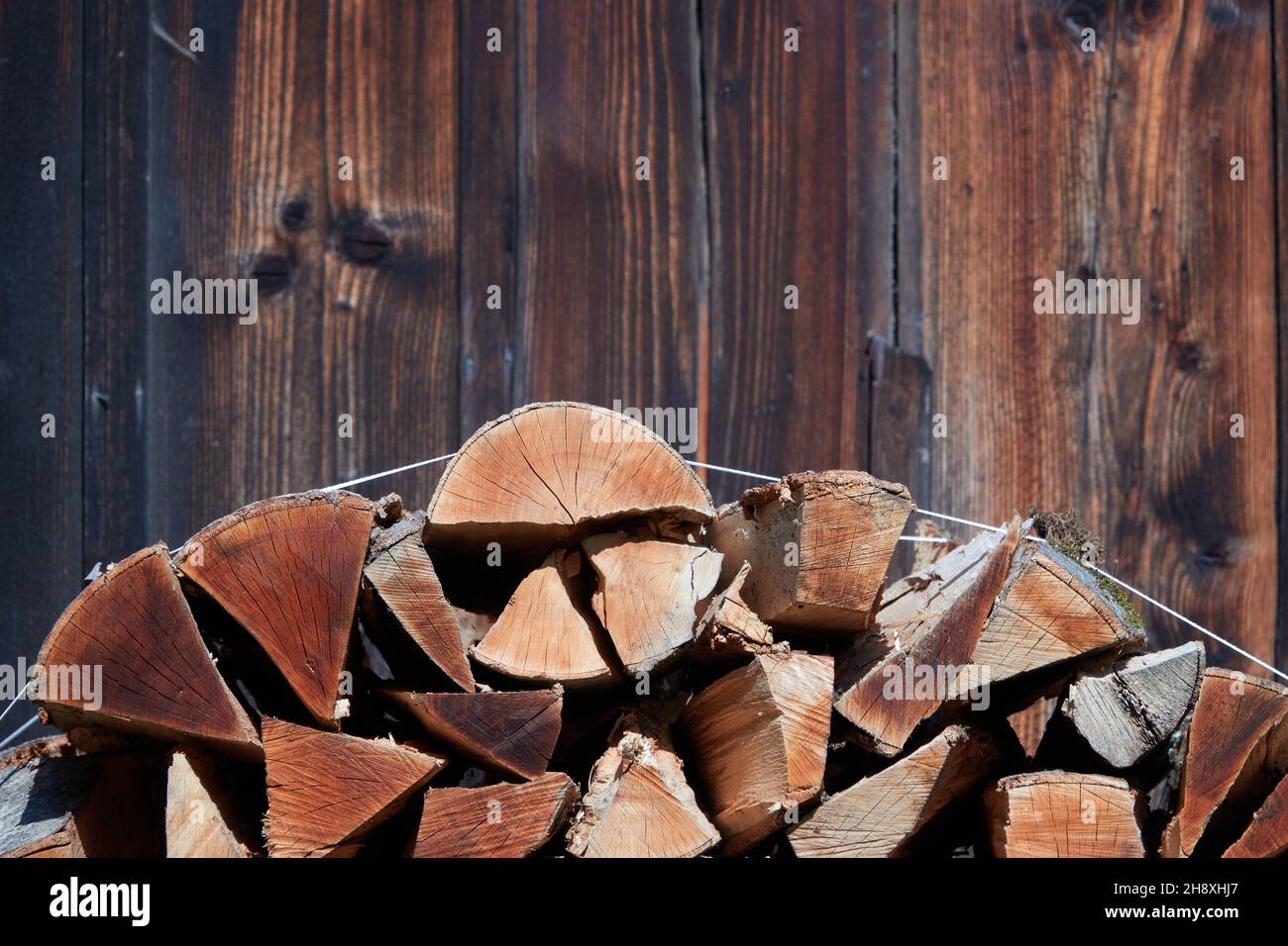 Firewood tied into a round bale, in the background dark wood panels ...