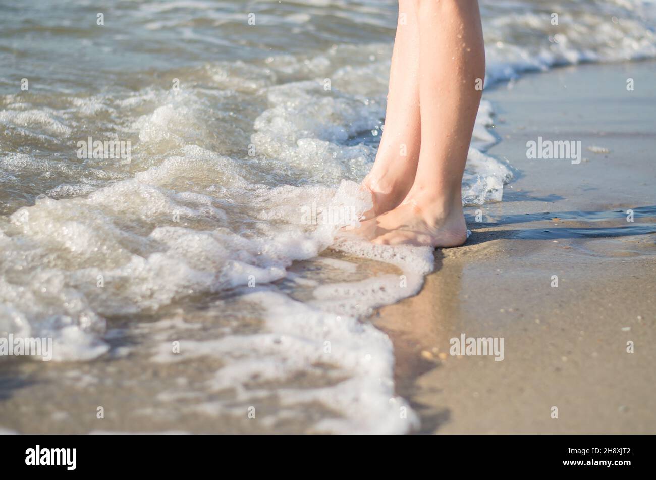Women's legs are covered by the sea wave. Feet in the water close-up ...