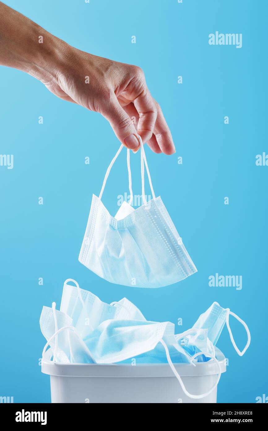 Hand throws a used face shield into the trash can on a light blue ...