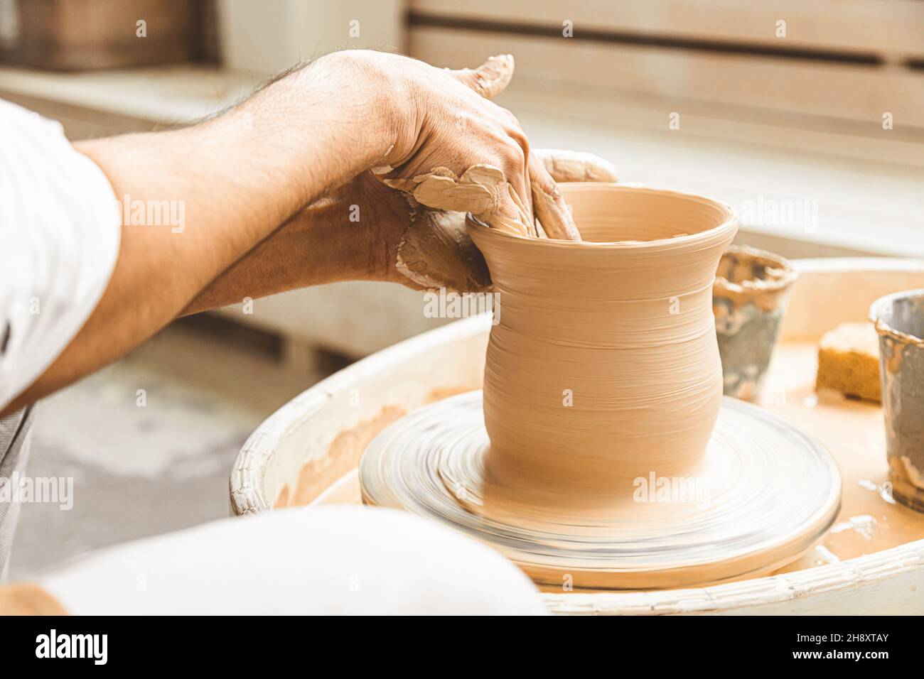 A young male potter works in his workshop on a potter's wheel and makes ...