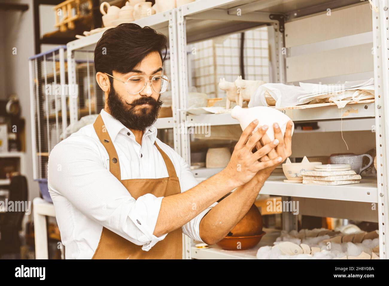 A young attractive male potter with a beard and mustache works in his ...
