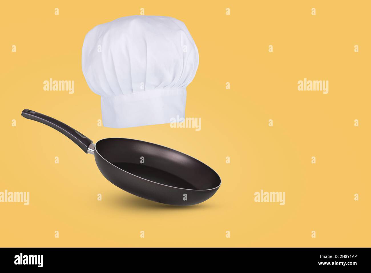 Frying pan and Chef hat floating in air isolated on a pastel yellow ...
