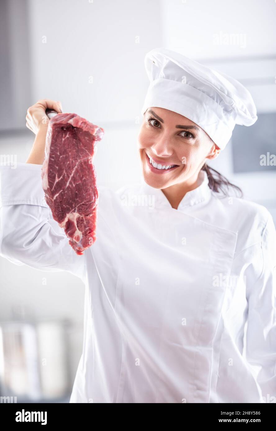 Female chef in professional white clothing holds a big chunk of beef ...