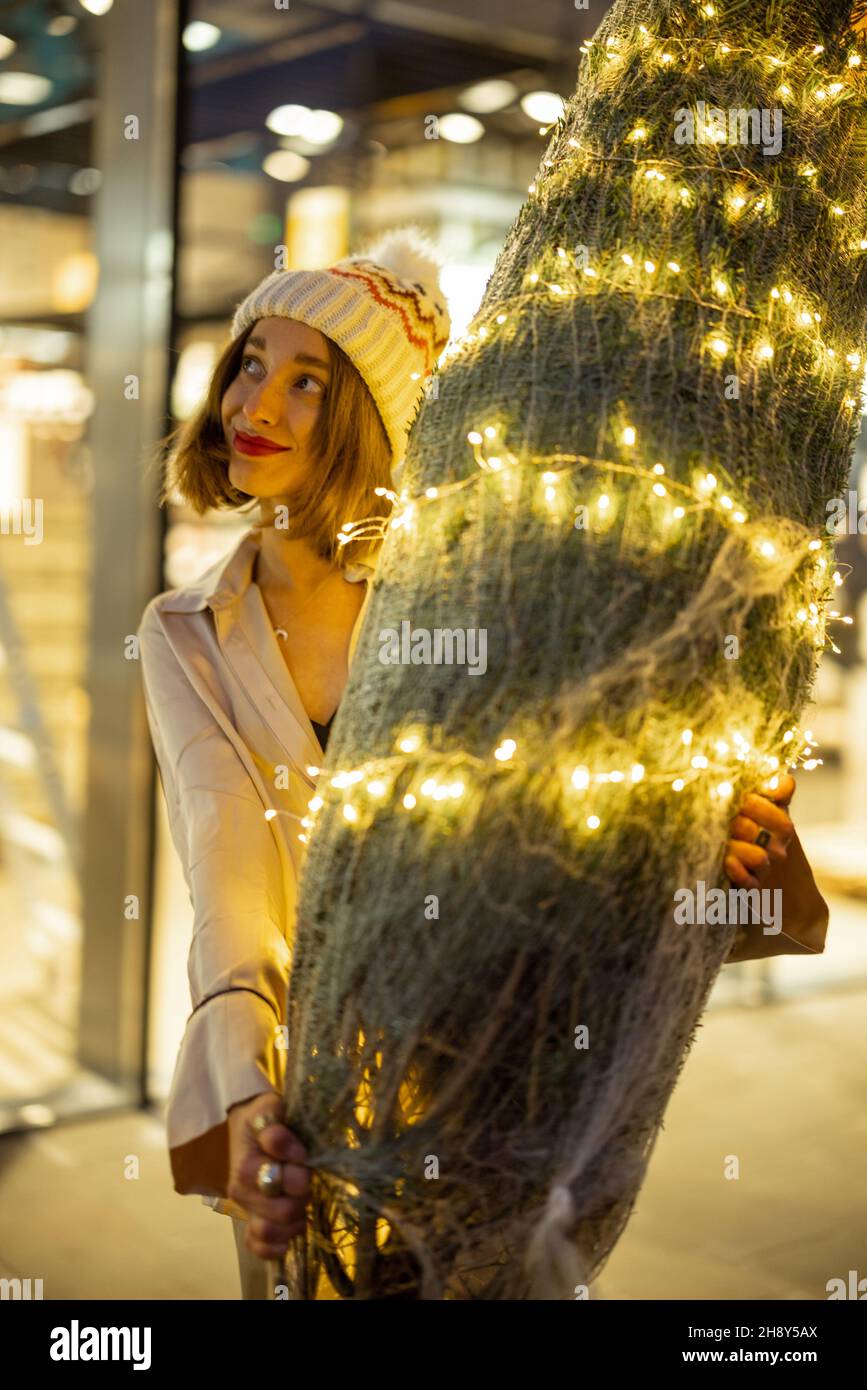 Woman carrying illuminated Christmas tree near the shopping centre ...