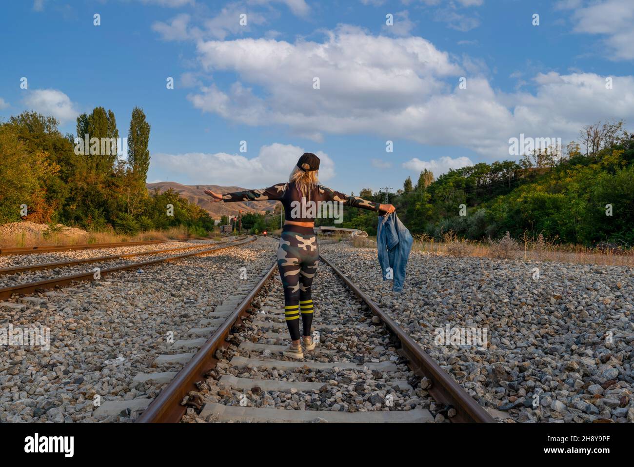 Rear view of woman stretching out her arms on railroad tracks. A woman ...