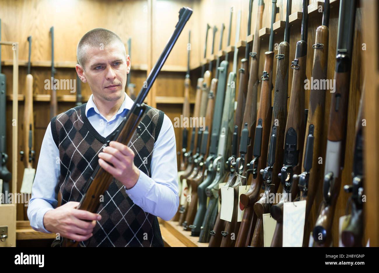 Interested man choosing hunting rifle in gun shop Stock Photo - Alamy