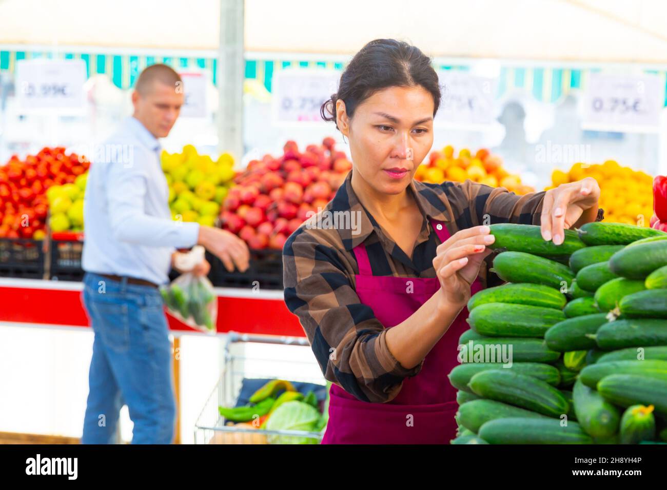 Supermarket worker putting cucumber on counter Stock Photo - Alamy