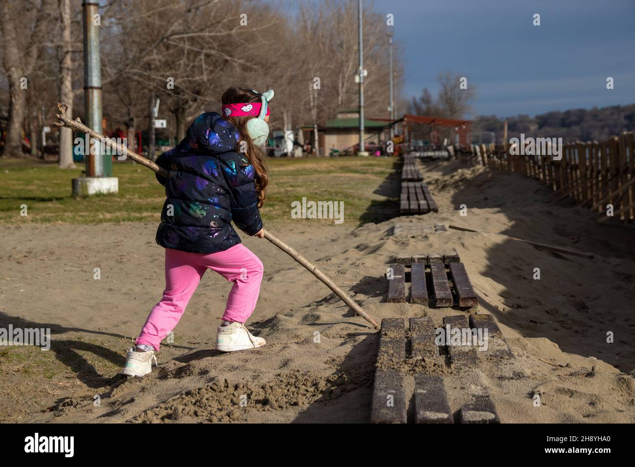 Rear view of a female holding stick pointing into the sand that almost ...