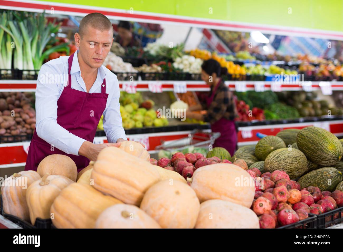 Salesman arranging fruits and vegetables on shelves at market Stock ...