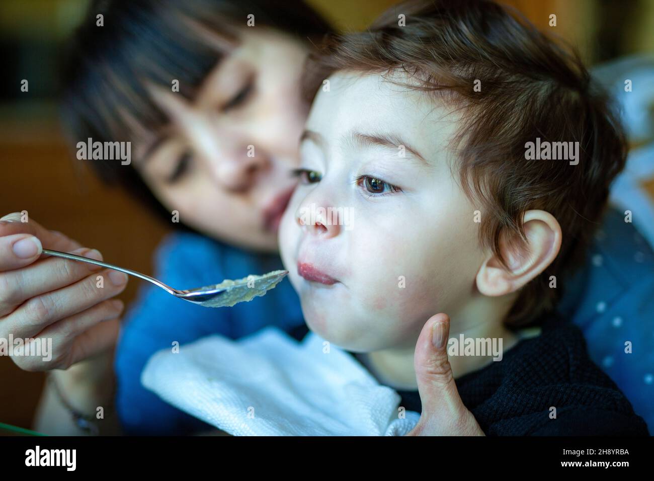 Asian mom feeding her baby toddler boy with a silver spoon as he has a ...