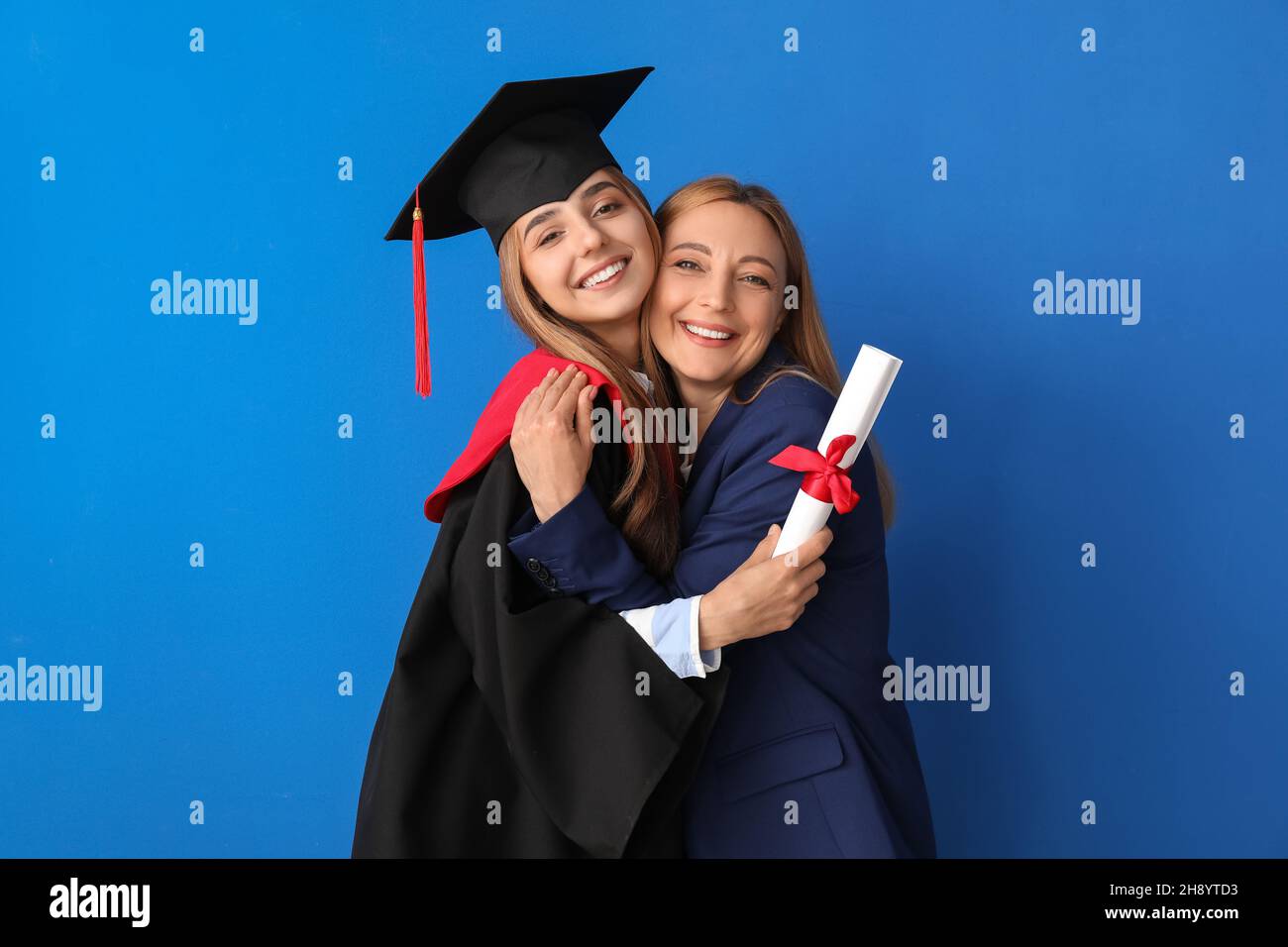 Happy female graduation student with her mother on color background ...
