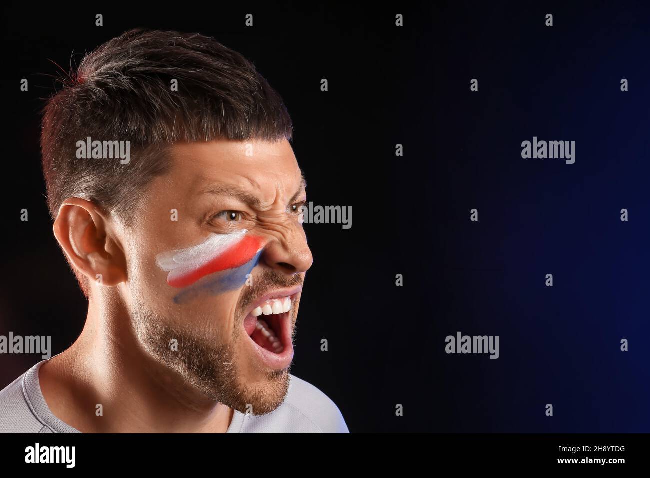 Aggressive man with flag of Russia painted on his face against dark ...