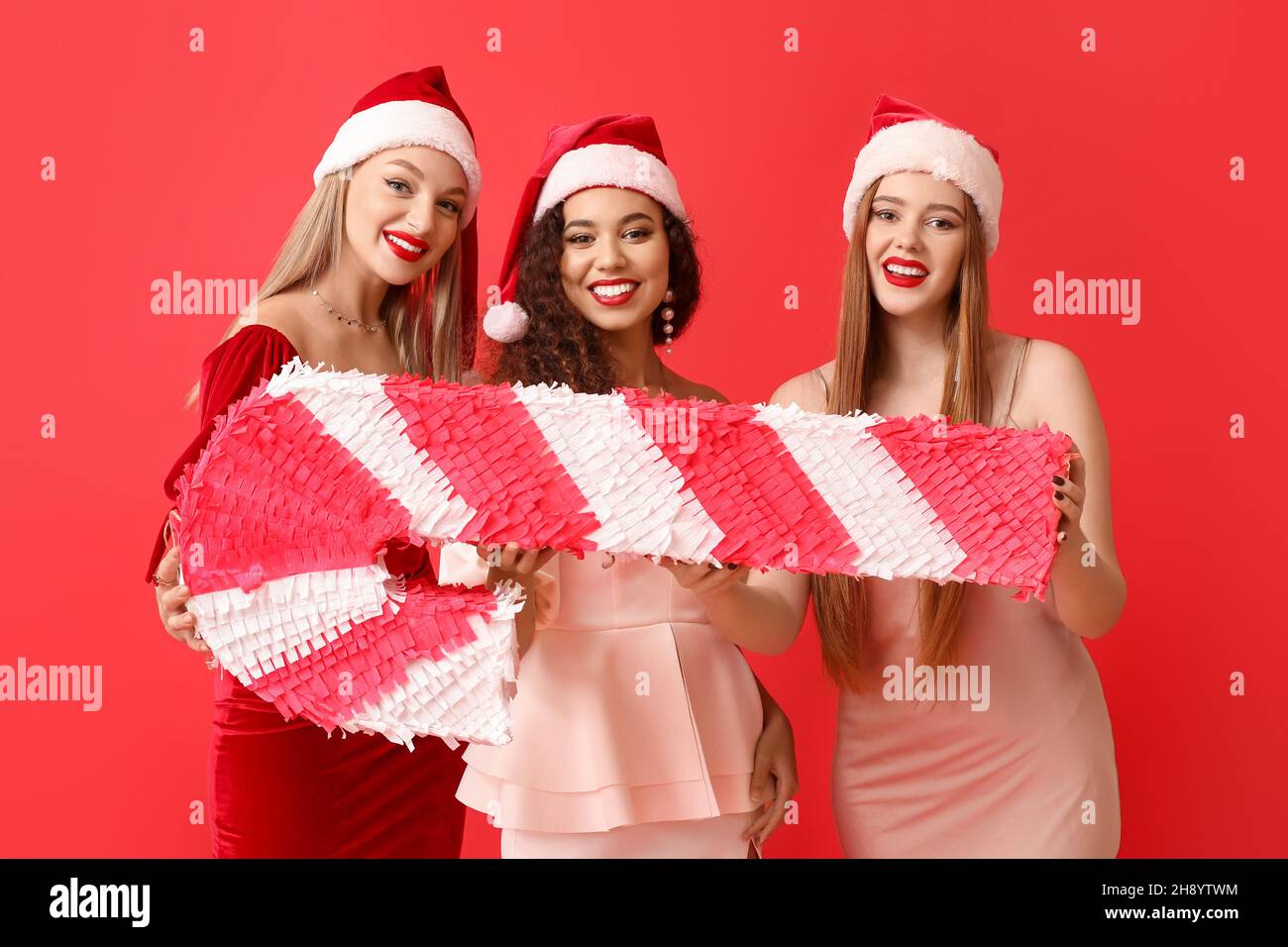 Beautiful young women in Santa hats and with candy cane pinata on color ...