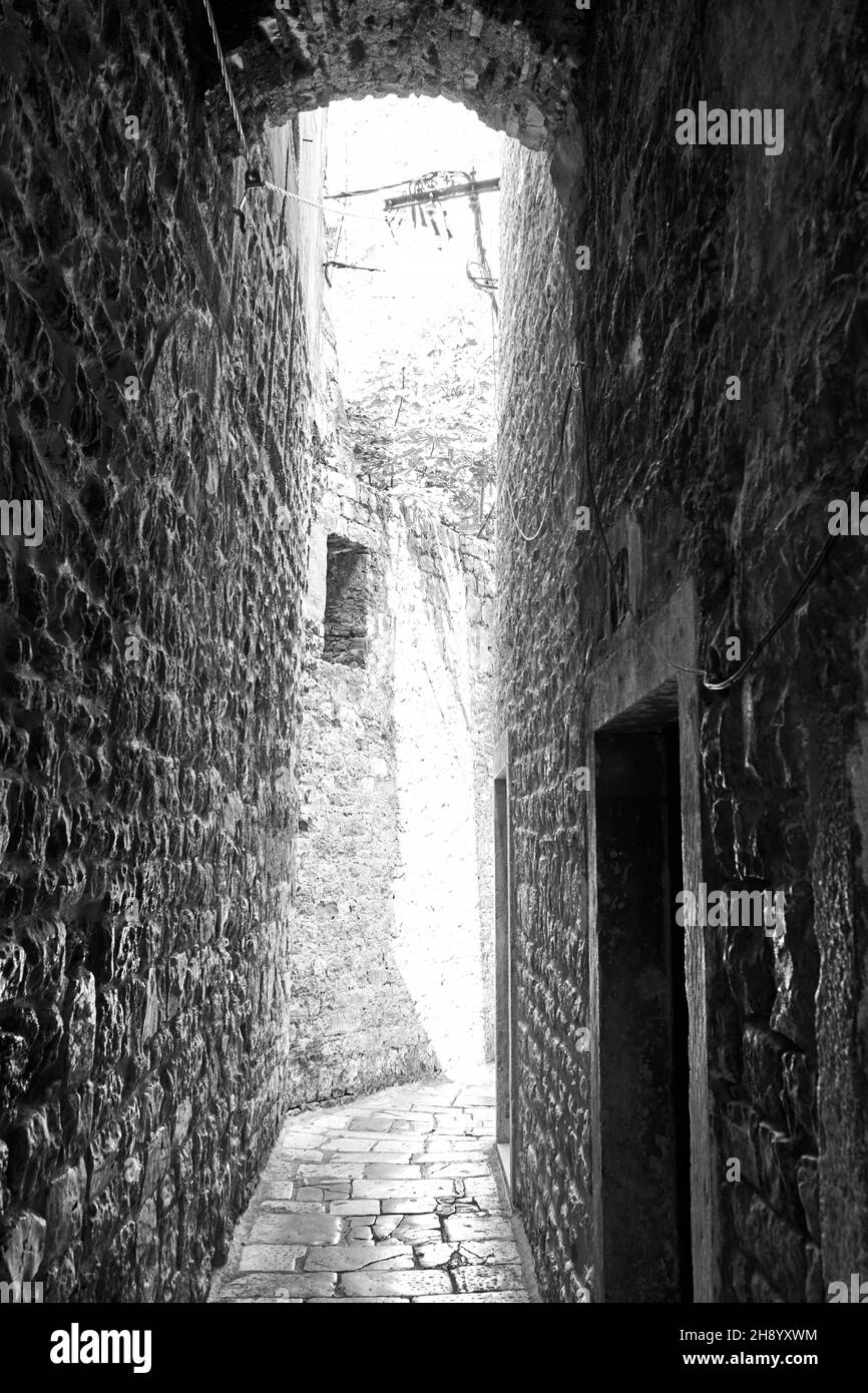 Vertical grayscale shot of narrow pathway between stone wall building ...
