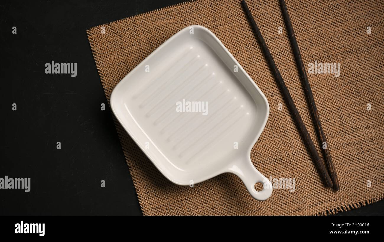 Modern white small pan plate with chopsticks on placemat over black ...