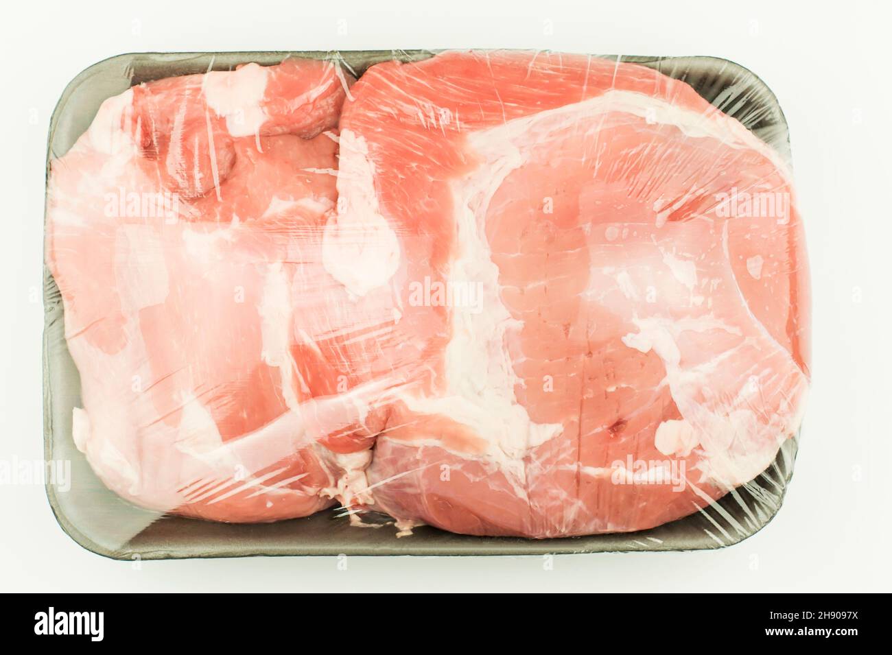 A large piece of raw pork meat packed hermetically on a black plastic ...