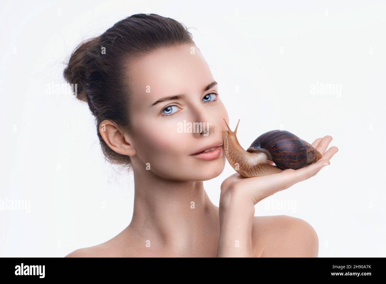 Beautiful young woman with snail on her face against white background ...