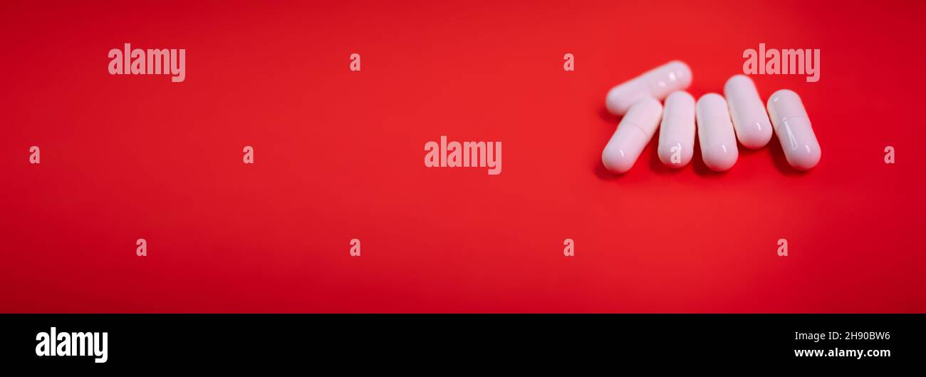 White drug capsules on colored red paper texture background. Macro ...