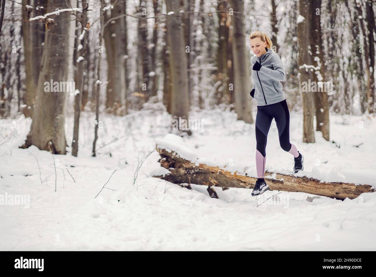 Happy fit woman jogging in woods at snowy winter day and jumping over ...