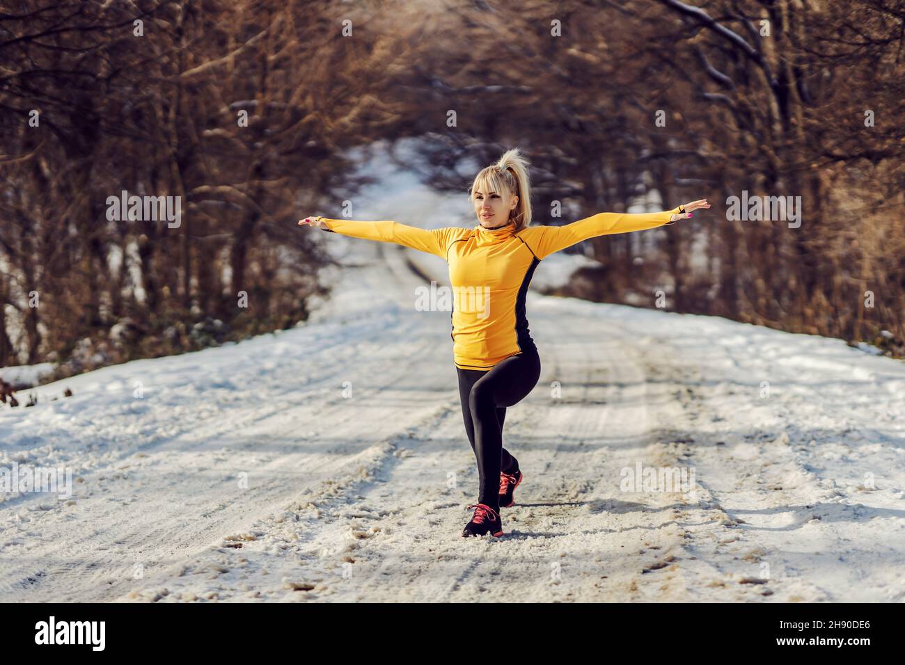 Fit sportswoman doing lunges on snowy path at sunny winter day. Warm up ...