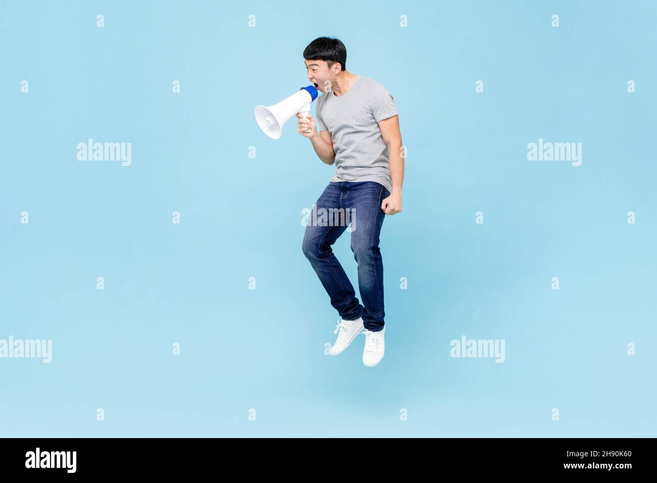 Young angry Asian man holding megaphone jumping and yelling in isolated ...