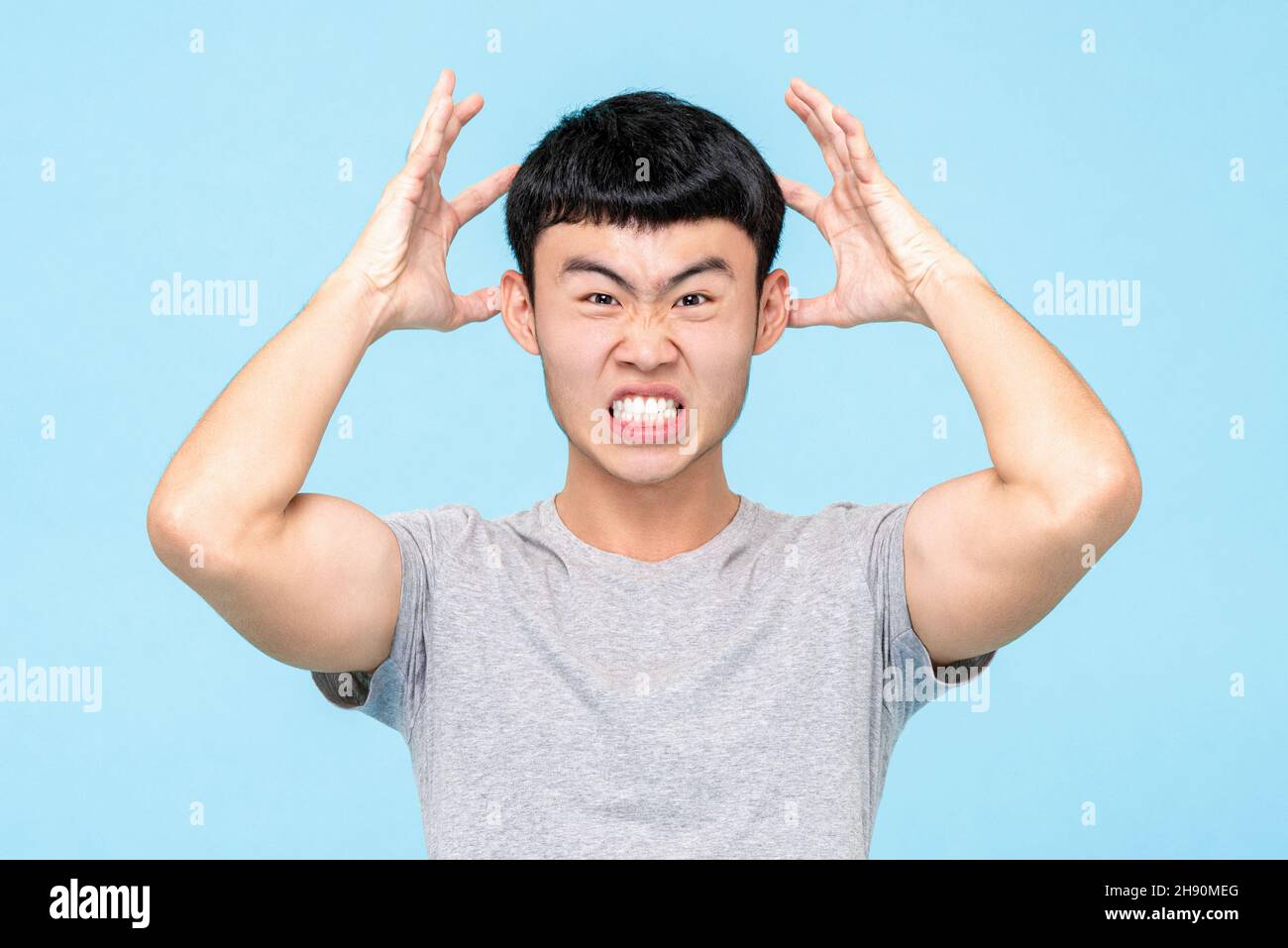 Young Asian man expressing angry emotion on isolated light blue studio ...