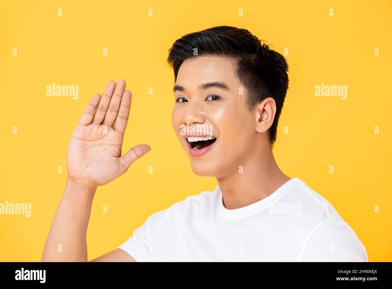 Young handsome Asian man waving hand and saying hi in isolated yellow studio background Stock ...