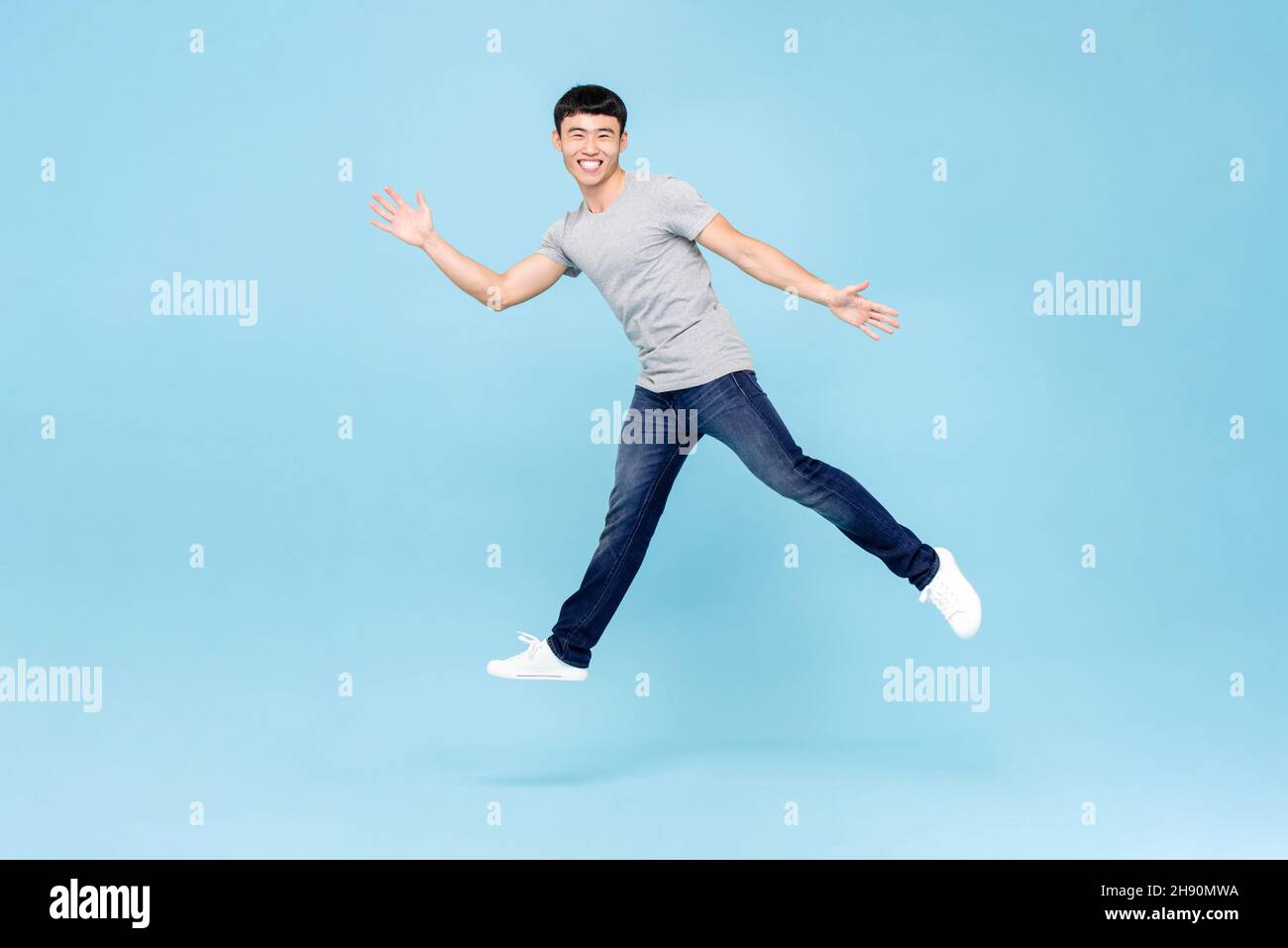 Jumping shot of ecstatic young Asian man with arms raising in mid air ...