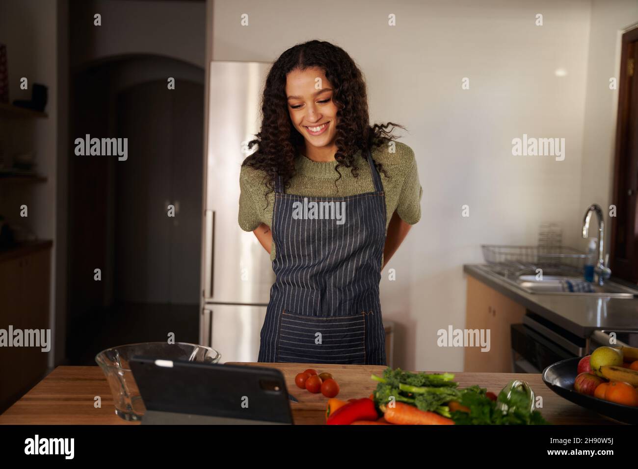 Multi-cultural young female reading recipe from tablet while cooking in ...
