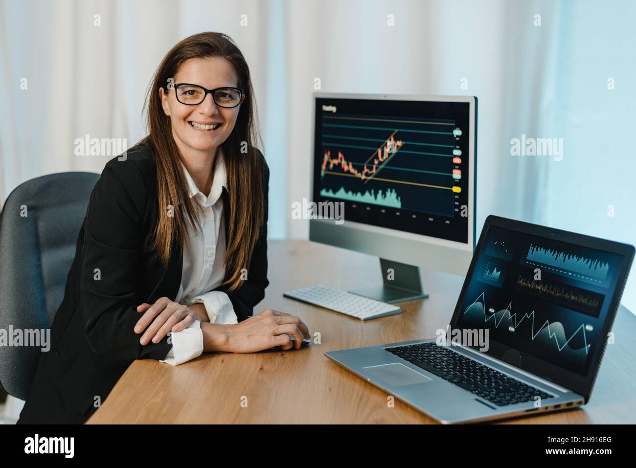 Female trader at table with laptop and computer monitor Stock Photo - Alamy