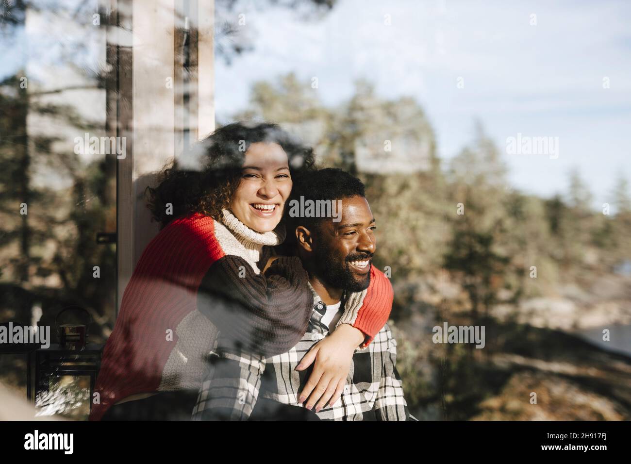Portrait of cheerful woman embracing boyfriend seen through window ...