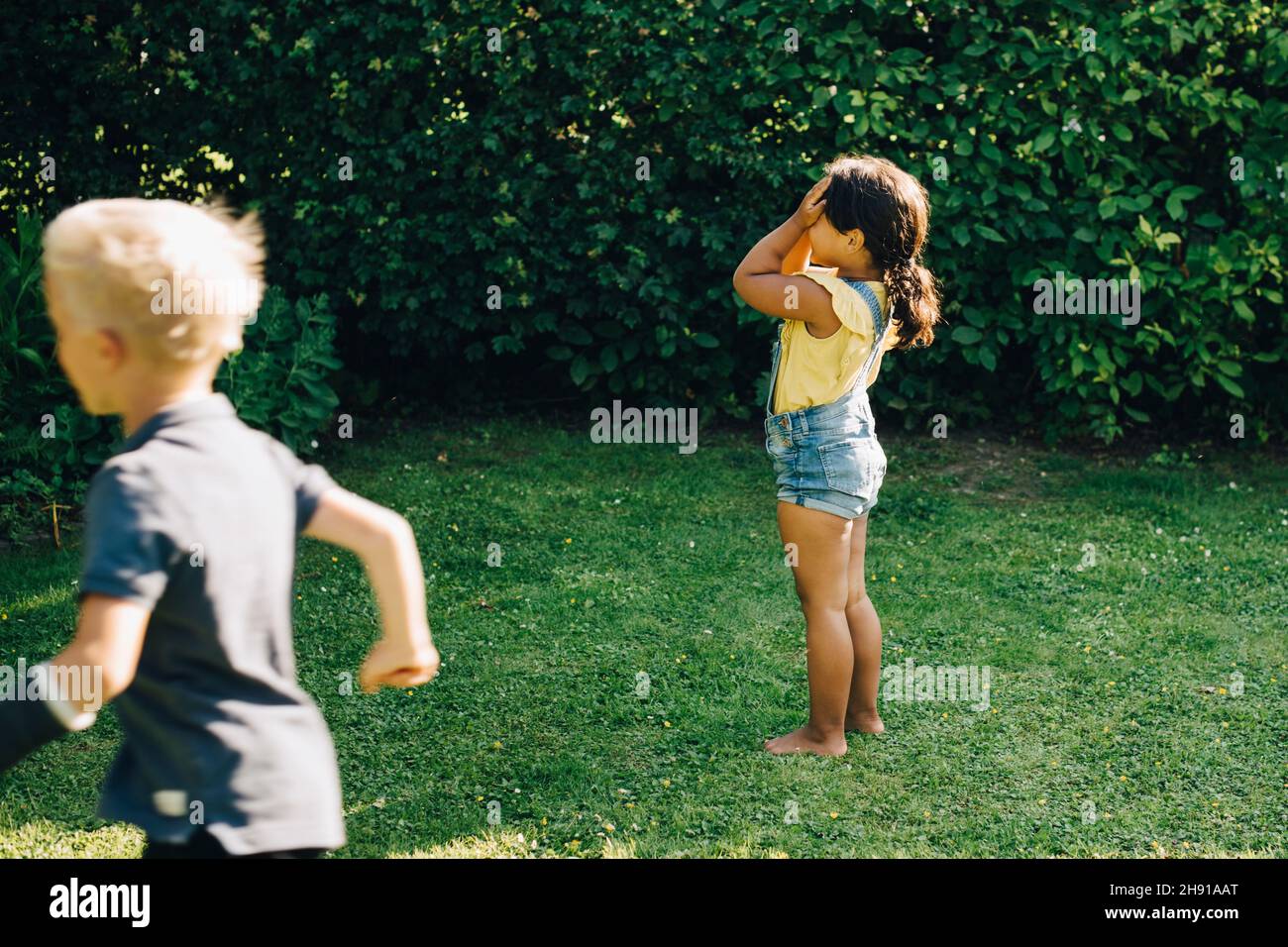 Boy running while playing hide and seek with female friend in backyard ...
