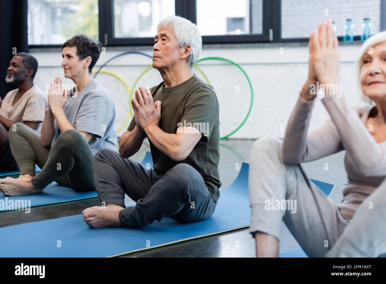 Barefoot asian man practicing yoga on mat near multiethnic people in ...