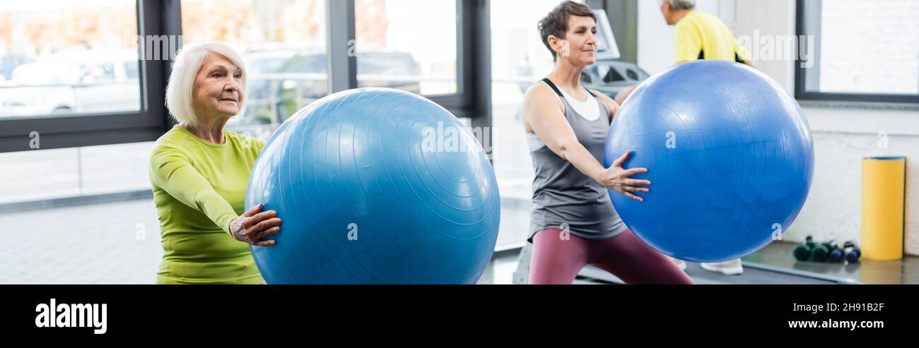 Grey haired sportswoman holding fitness ball in sports center, banner ...