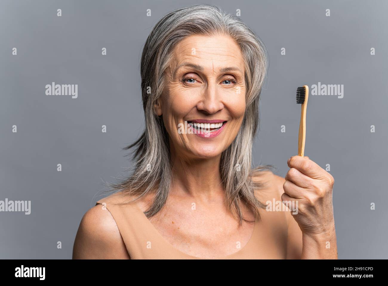 Dental care concept. Smiling mature lady with gray silver hair looks at ...