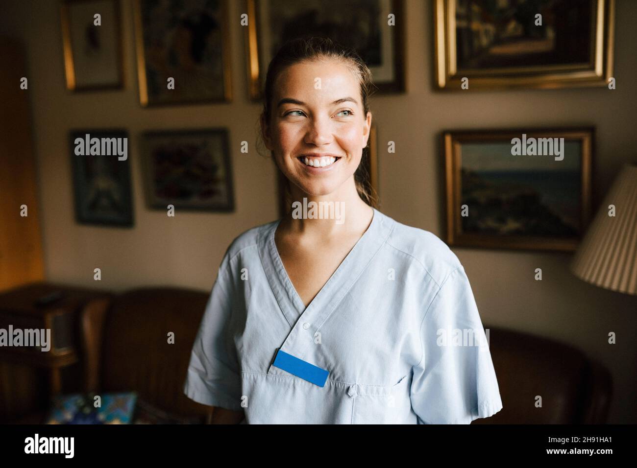 Happy female nurse looking away in living room Stock Photo - Alamy