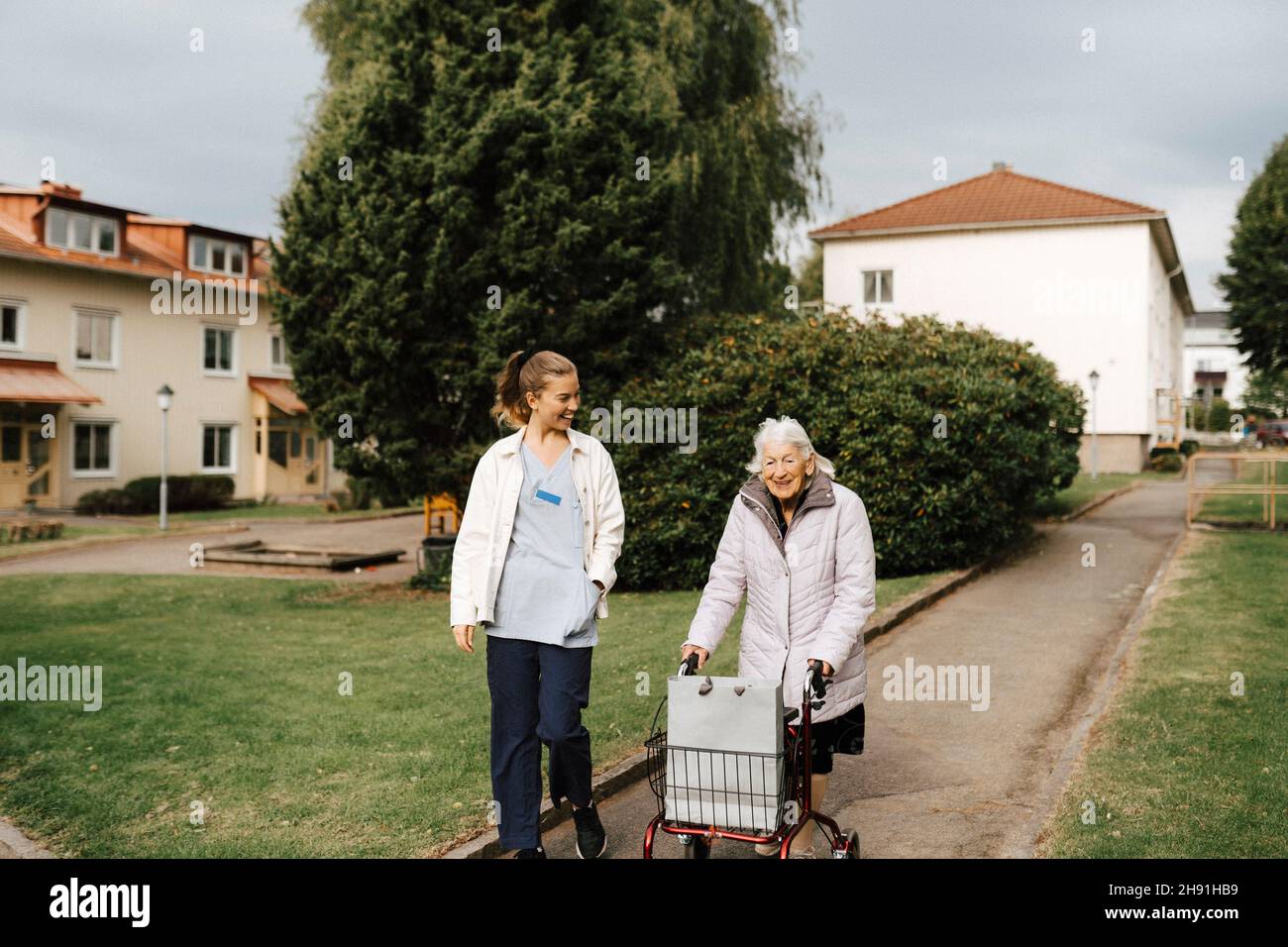 Smiling female healthcare worker looking at senior woman with walker on ...