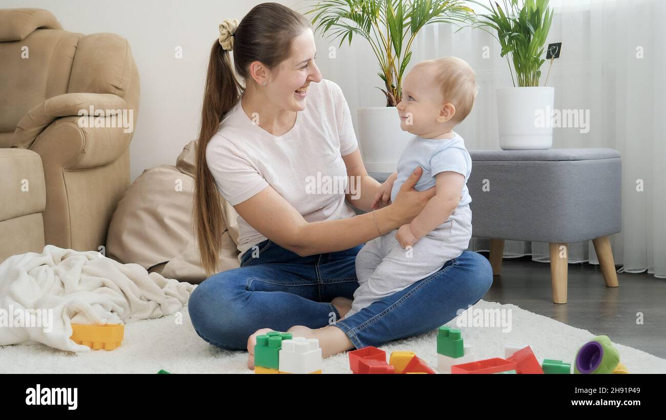 Cute smiling baby boy sitting on mothers lap and looking on colorful ...