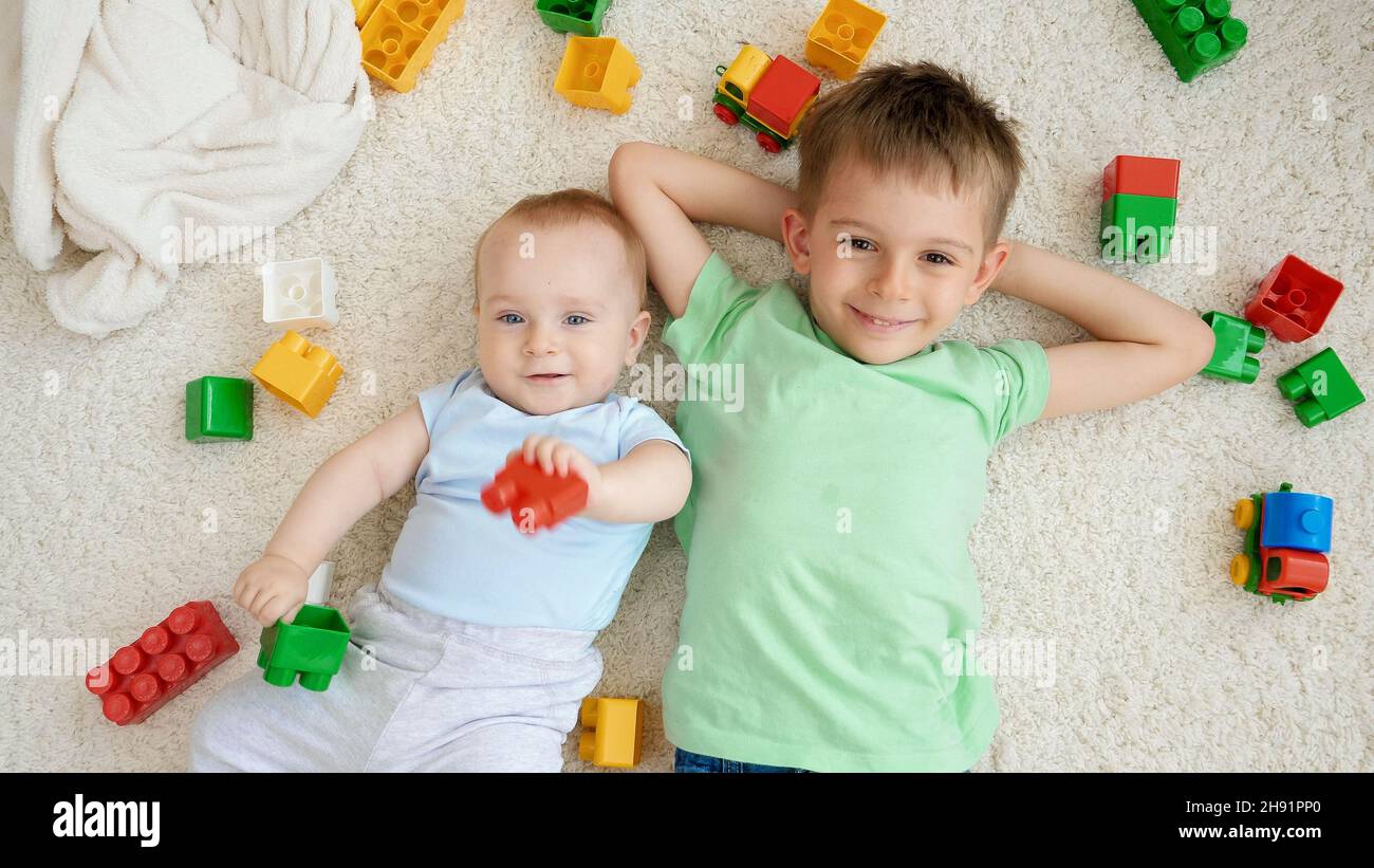 Portrait of smiling baby boy with older brother playing toy bricks and ...