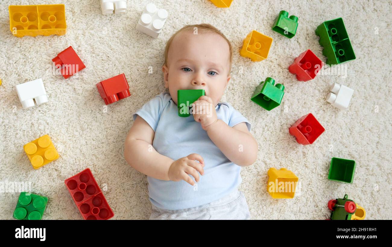 Portrait of little baby boy chewing and biting colorful toys while hes ...
