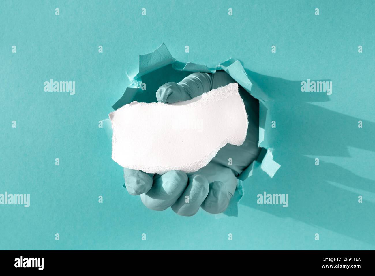 Hand in glove through paper hole holding torn piece of paper. Copy ...