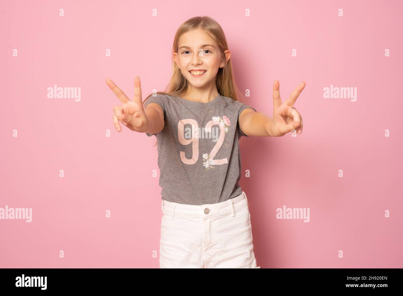 Happy cute little girl standing and showing peace symbol over pink ...