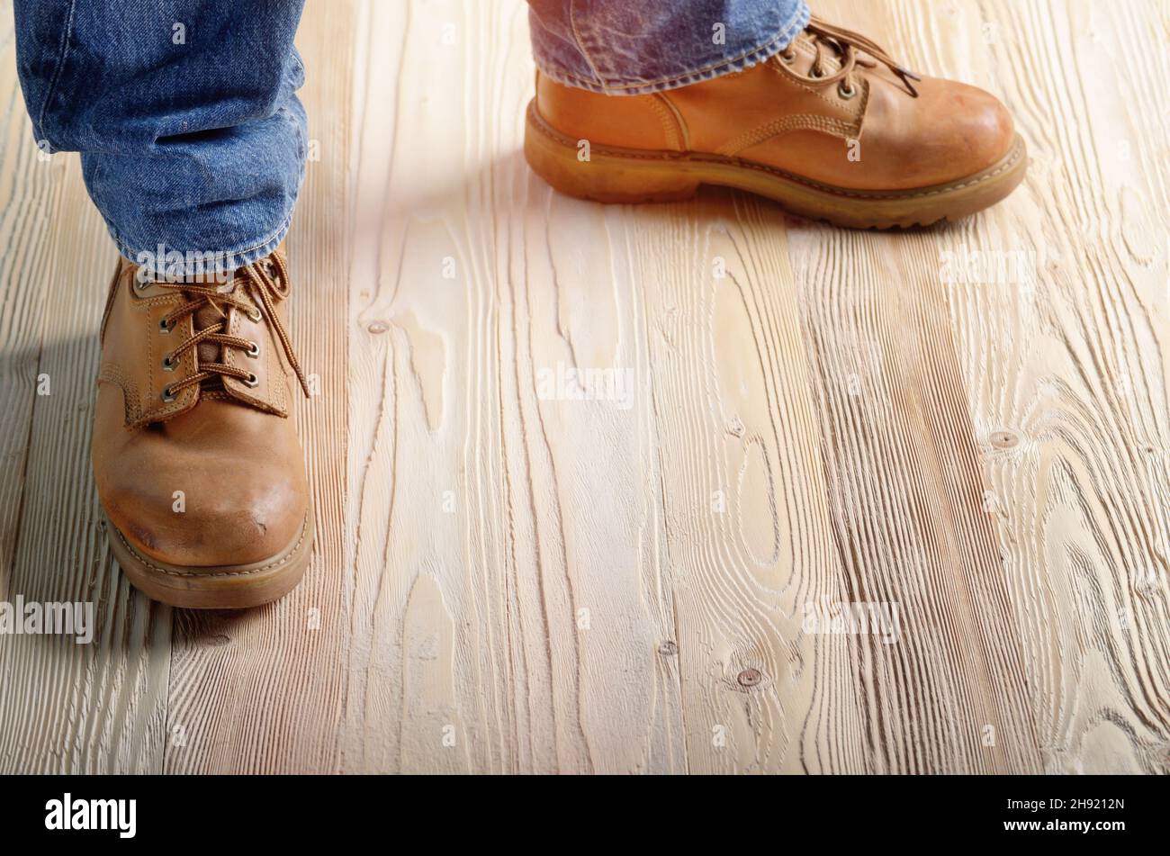 Carpenter feet in work boots standing on wooden floor. Place for text ...