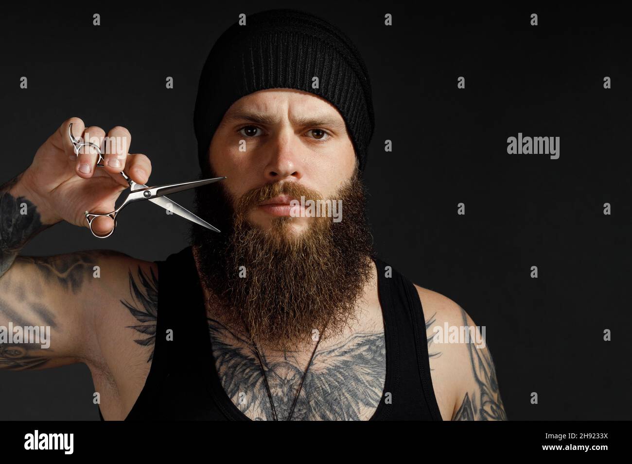 portrait of a courageous man with a beard he holds scissors near his ...