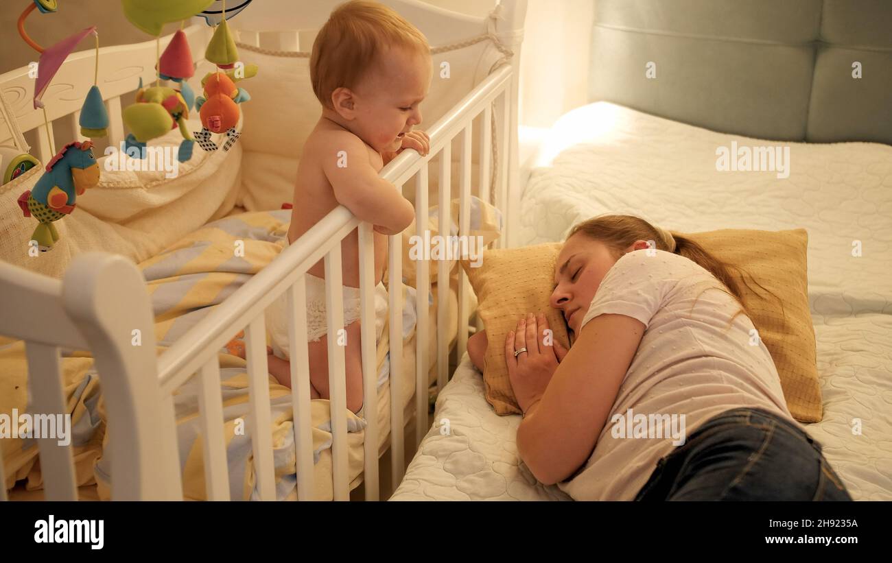 Young tired mother fell asleep next to her baby crying in bed. Concept ...
