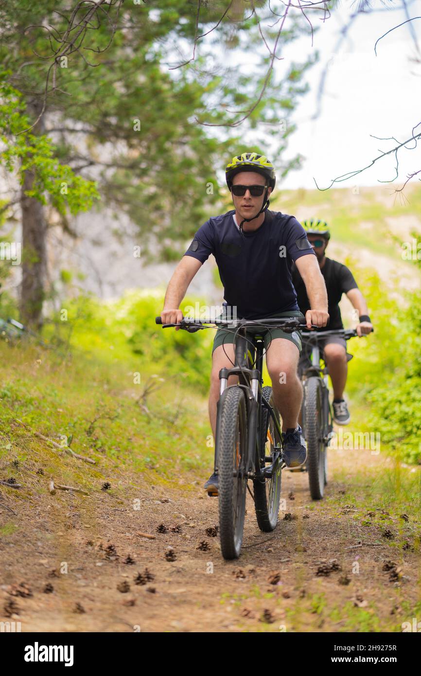 Two handsome male friends are riding a bike together in the forest ...